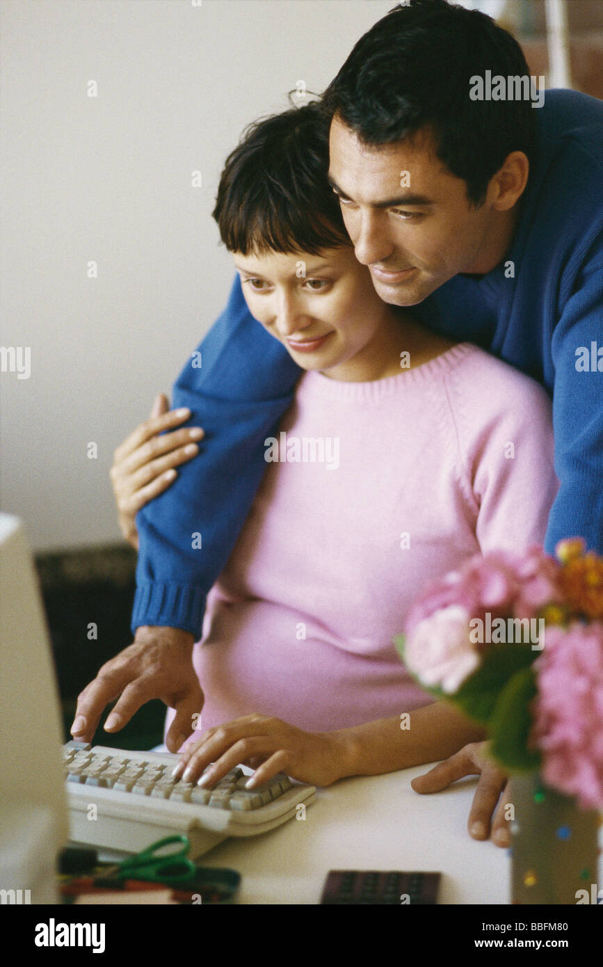 Couple typing on keyboard together, man leaning over woman's shoulder ...