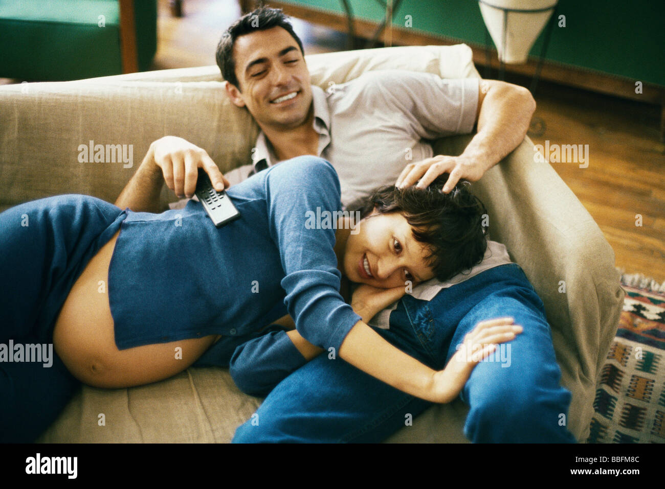 Expecting couple relaxing on sofa, watching TV, woman resting head in ...