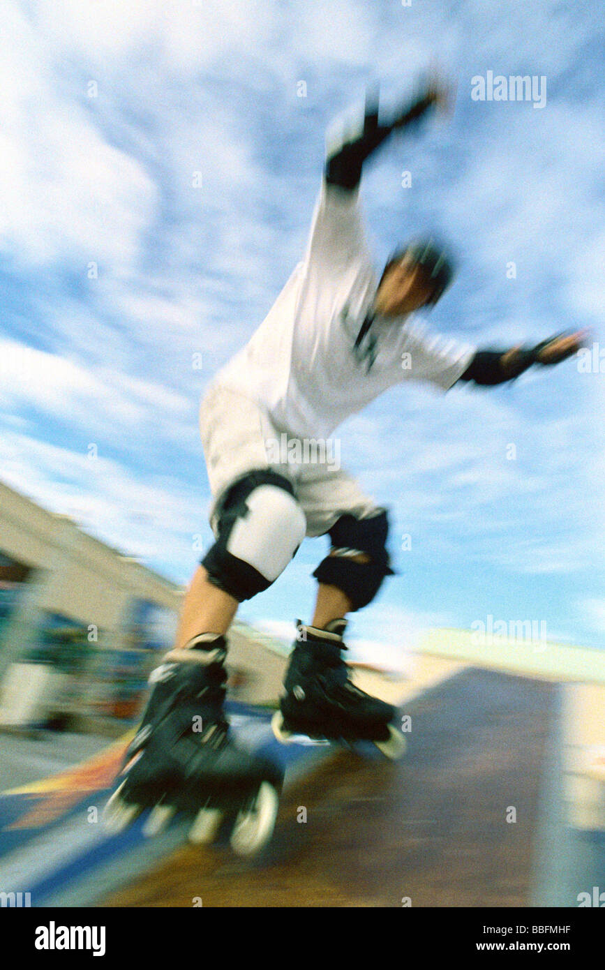 Inline skater with arms raised sliding on ramp at skatepark Stock Photo ...