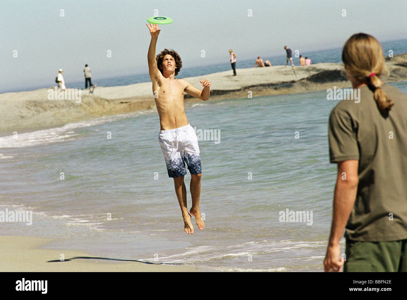 Two friends on beach throwing frisbee, one jumping to catch Stock Photo ...