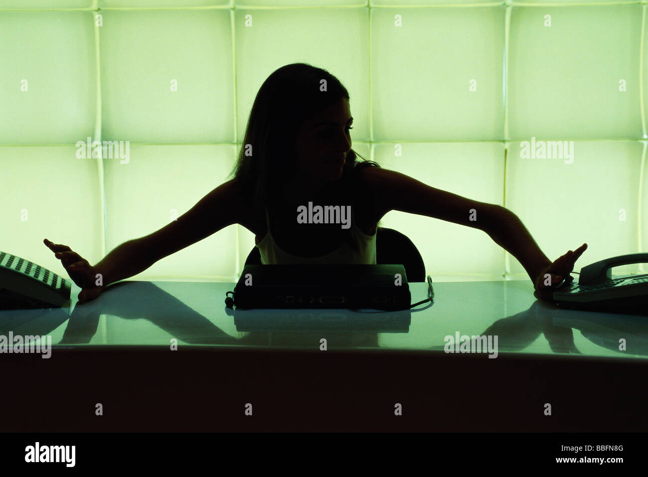Woman seated at desk reaching for two ringing phones Stock Photo - Alamy