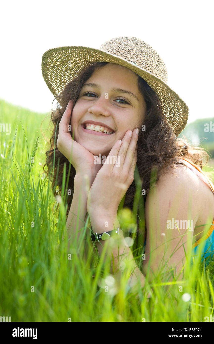 Portrait Of A Smiling Girl Wearing A Sun Hat While Lying On A Meadow