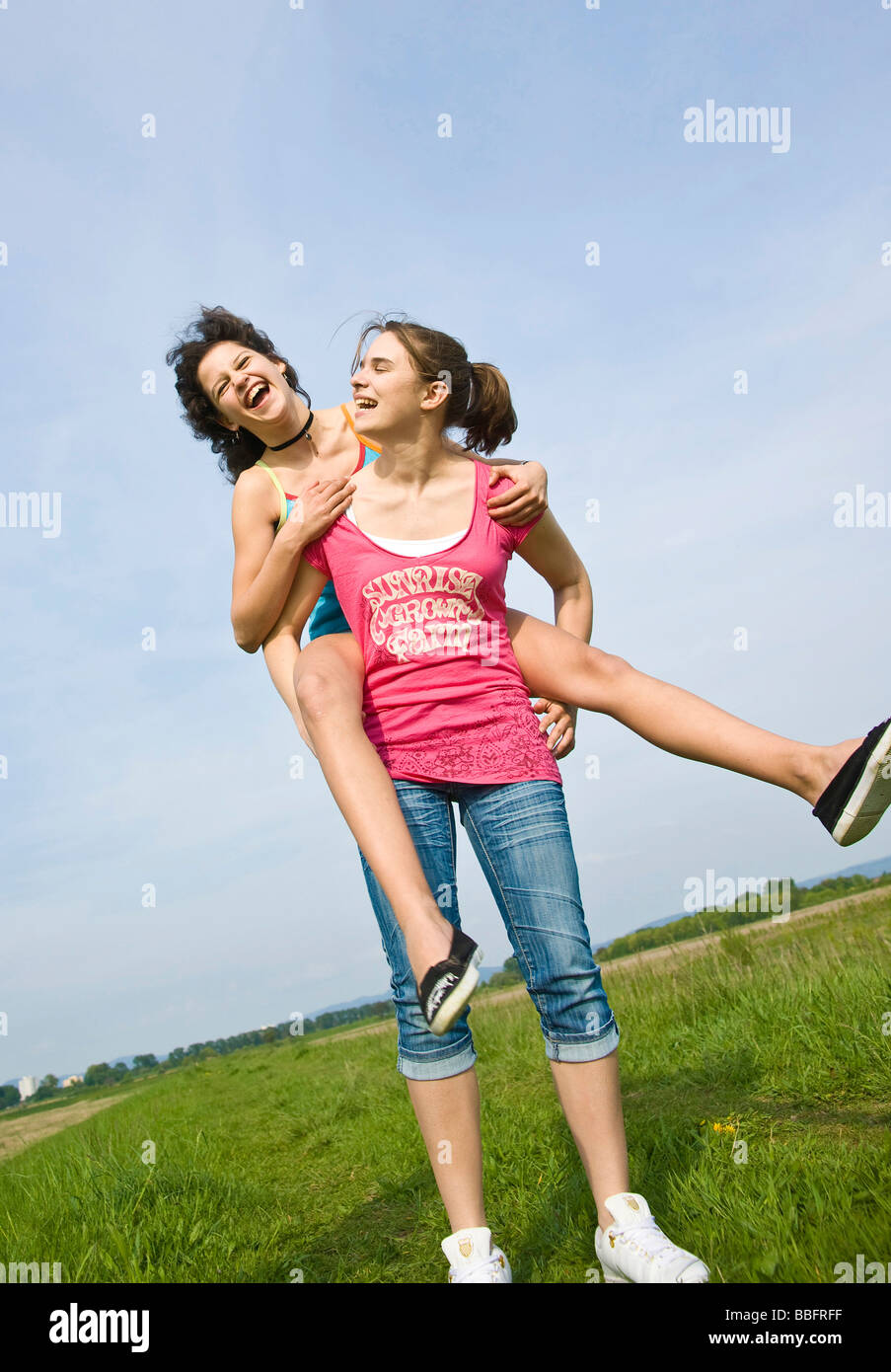 Girl carrying her friend piggy-back over a meadow Stock Photo - Alamy