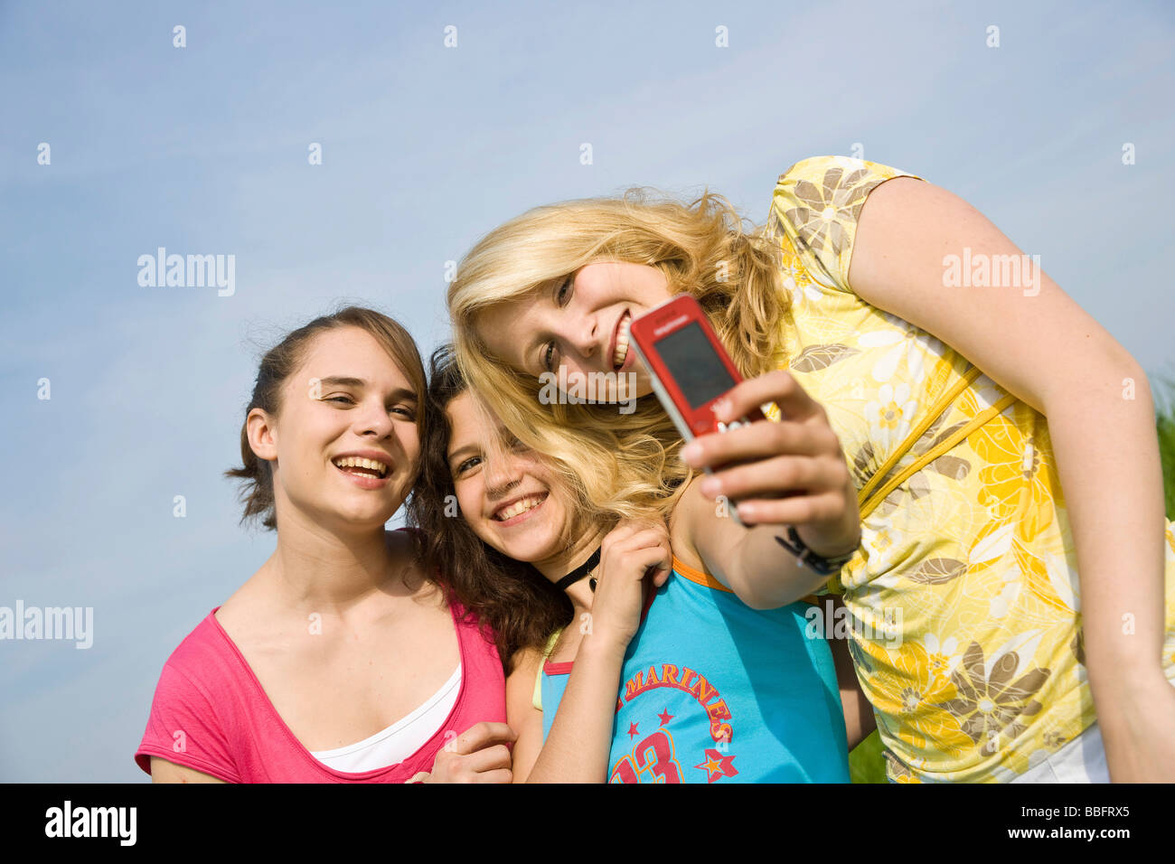 Three smiling girls taking a photo of themselves with a mobile phone ...