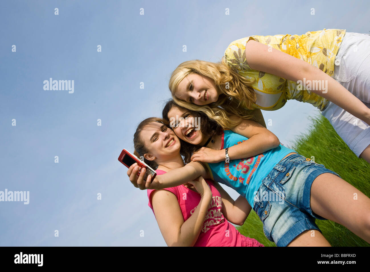Three smiling girls taking a photo of themselves with a mobile phone ...