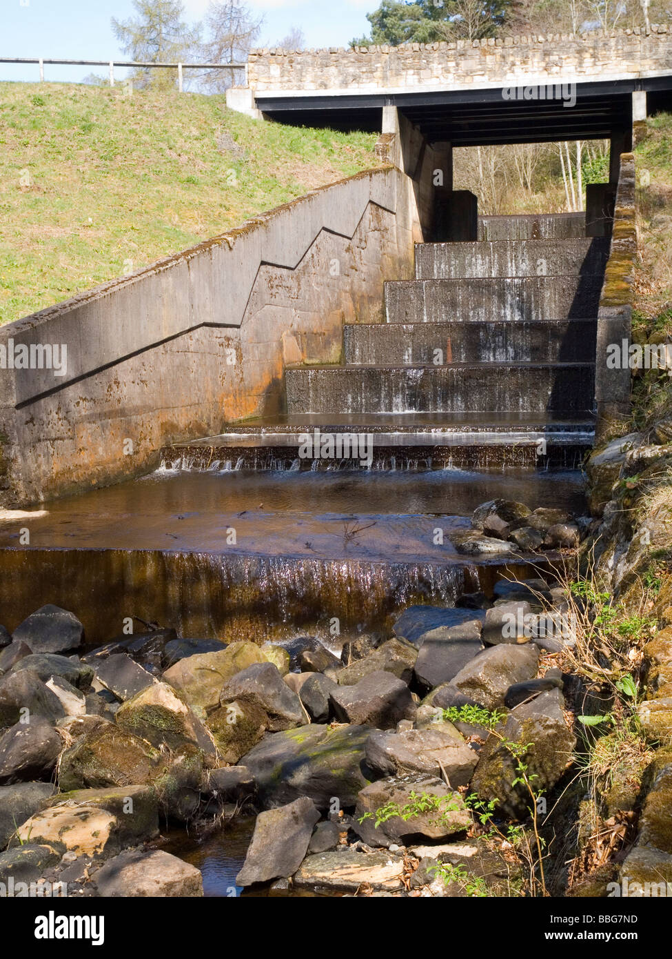 A weir running down beneath a bridge into a rocky stream Stock Photo ...