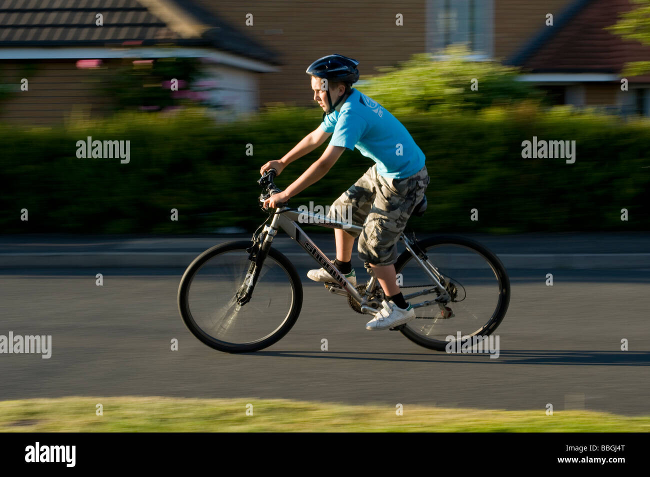 Young teenage boy riding a bicycle at speed along a suburban street in ...