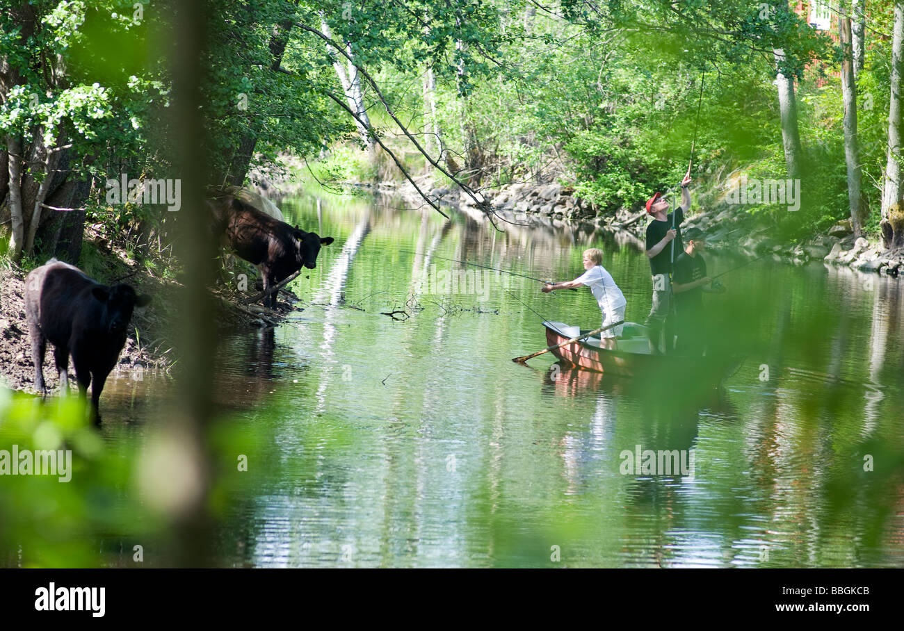 Three persons fishing from a rowing boat on a river in southern Sweden ...