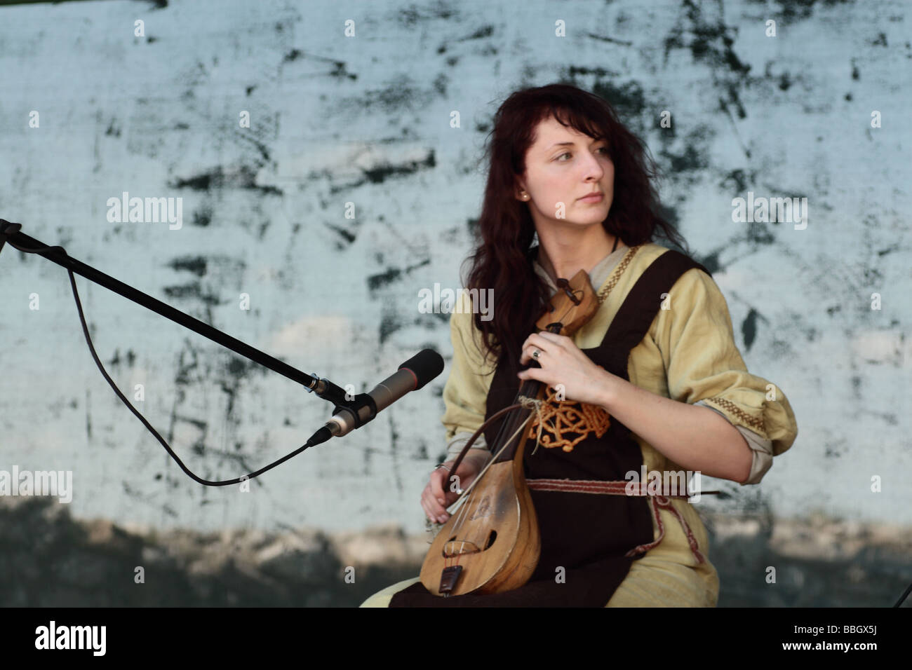 Female folk musician playing ancient violin on stage with microphone ...