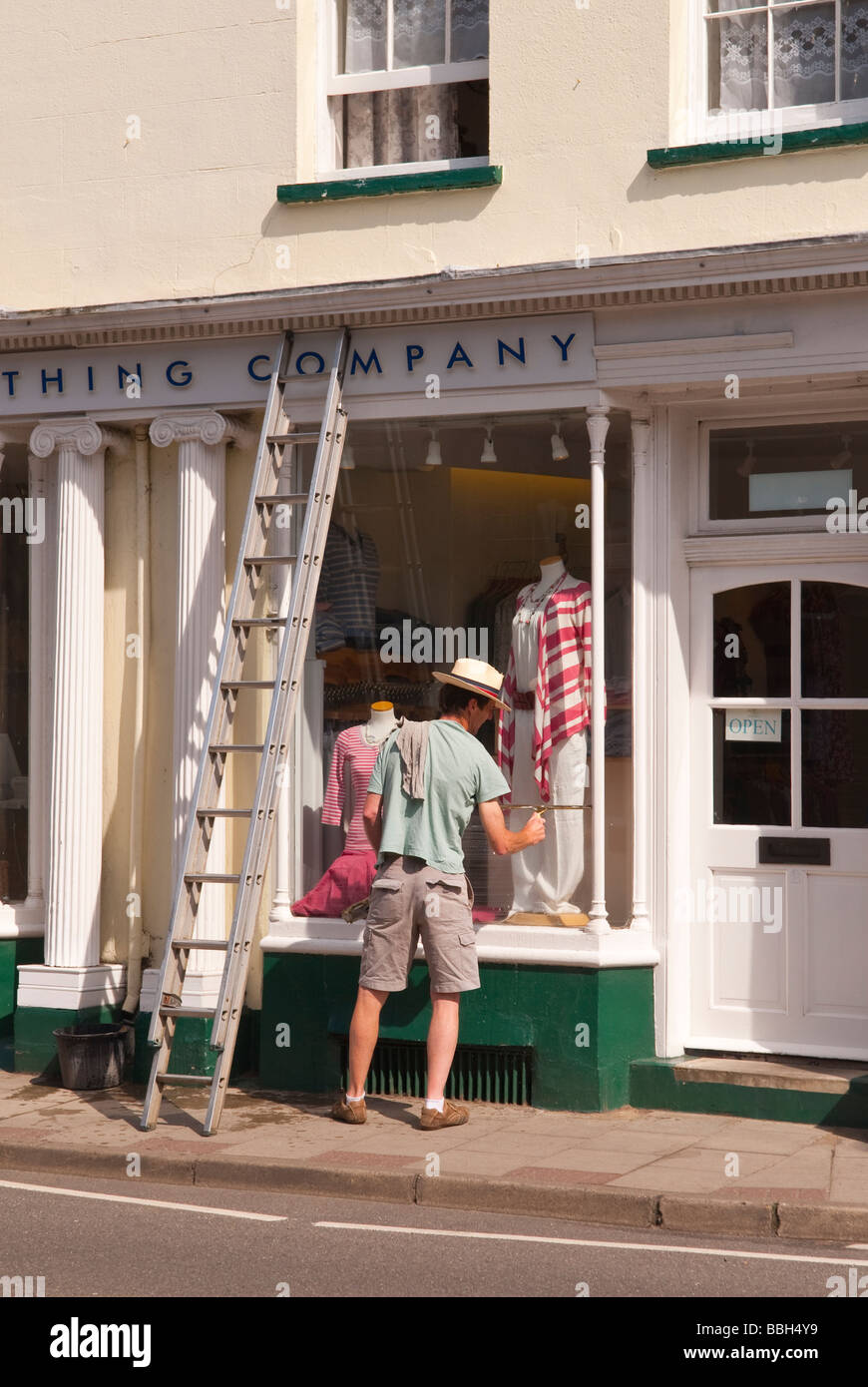 A window cleaner cleaning the windows of a shop with his ladder beside ...