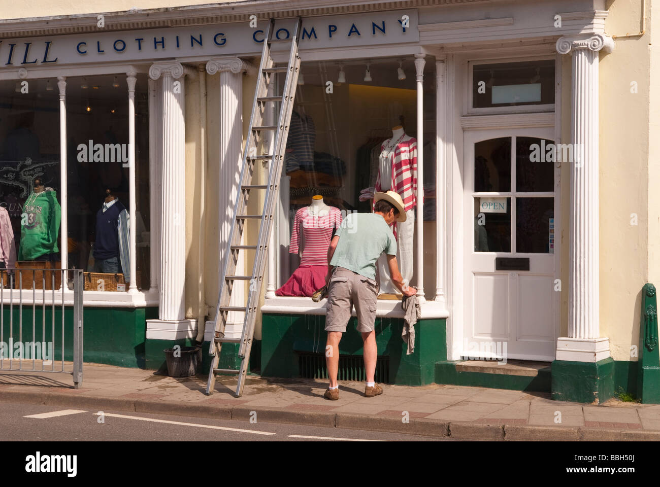 A window cleaner cleaning the windows of a shop with his ladder beside ...