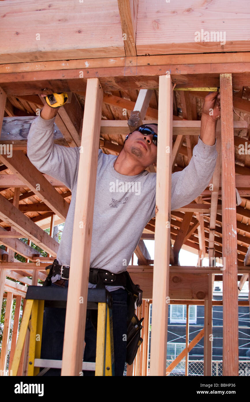 Carpenter on ladder measuring length of wood with measuring tape on a ...