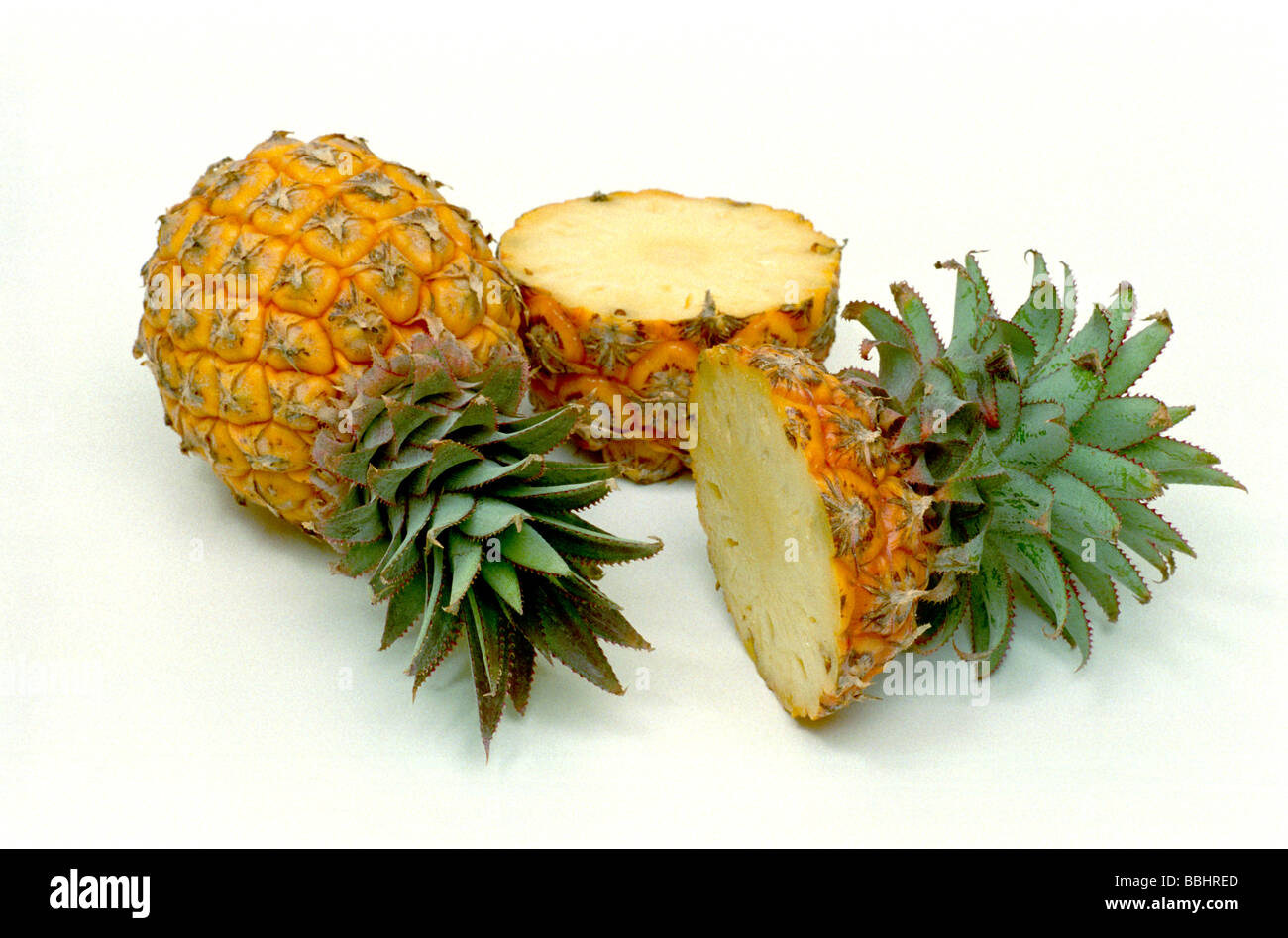 Two Pineapples on a plain background, one whole and the other cut in ...