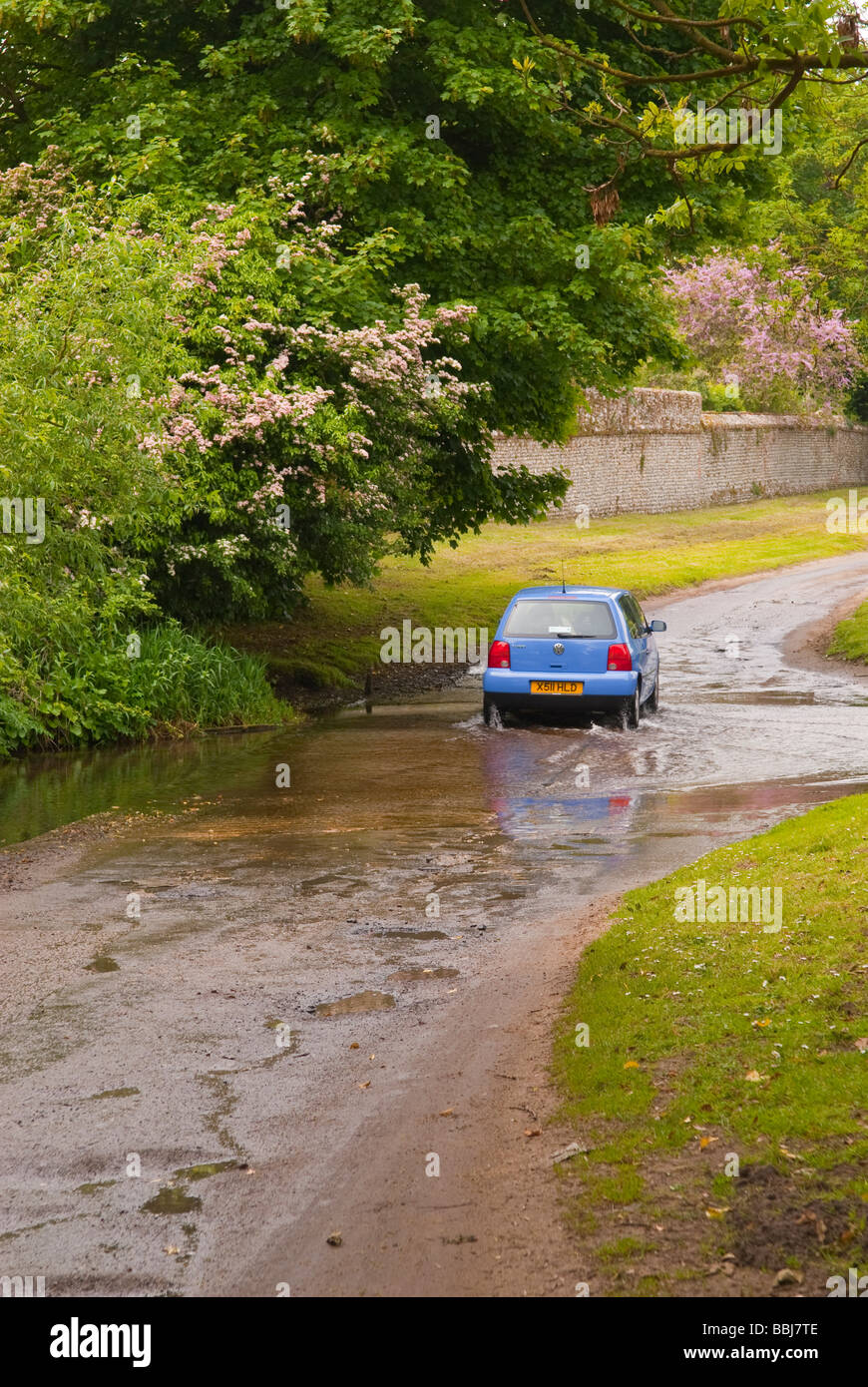 A car driving through a ford running across a country lane in the Uk ...