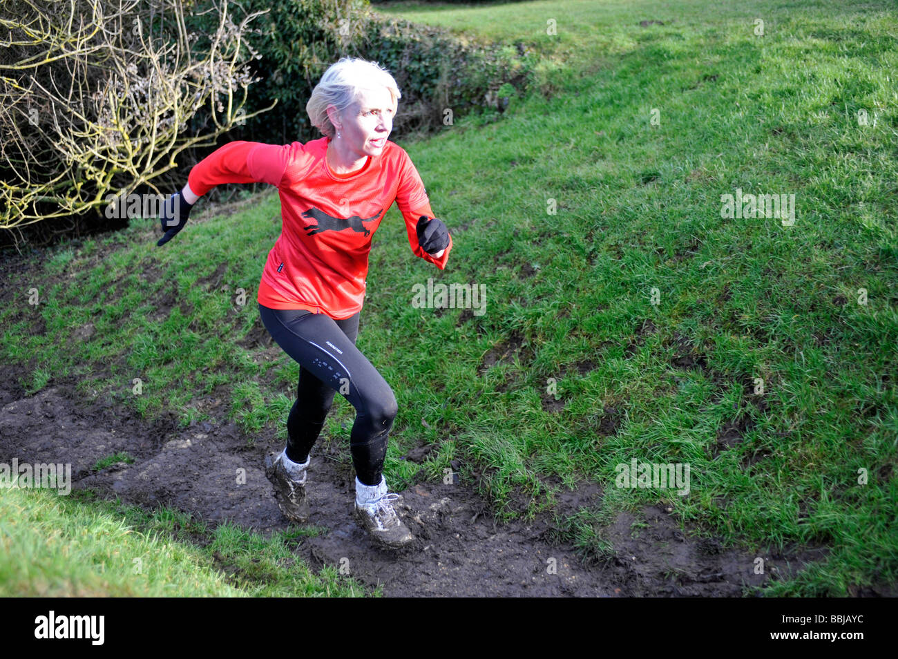 middle aged female club runner running up muddy slope during club event ...