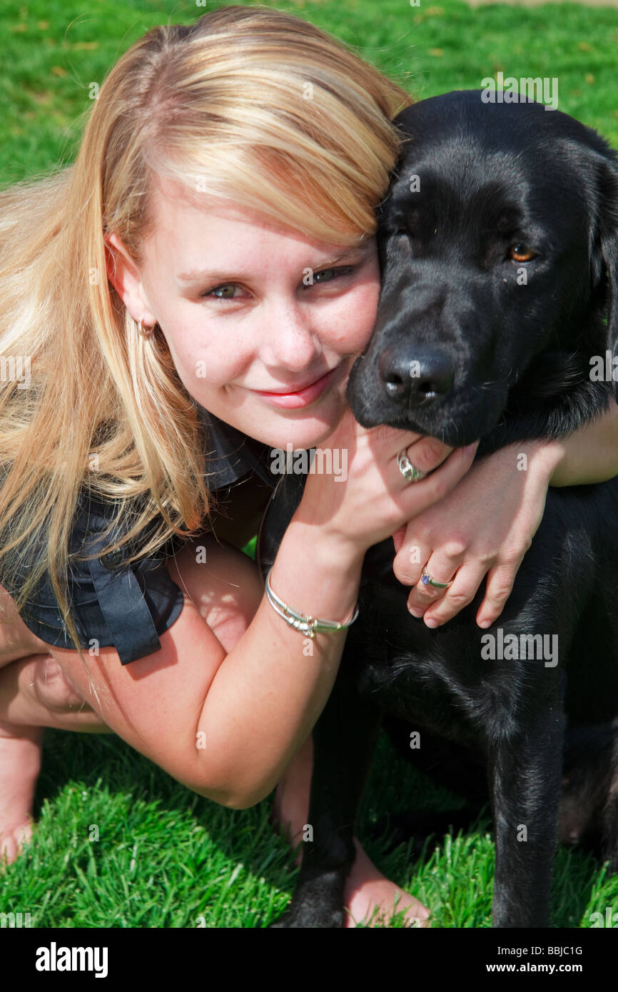 Young white blond woman girl with hugging her black Labrador puppy pet ...