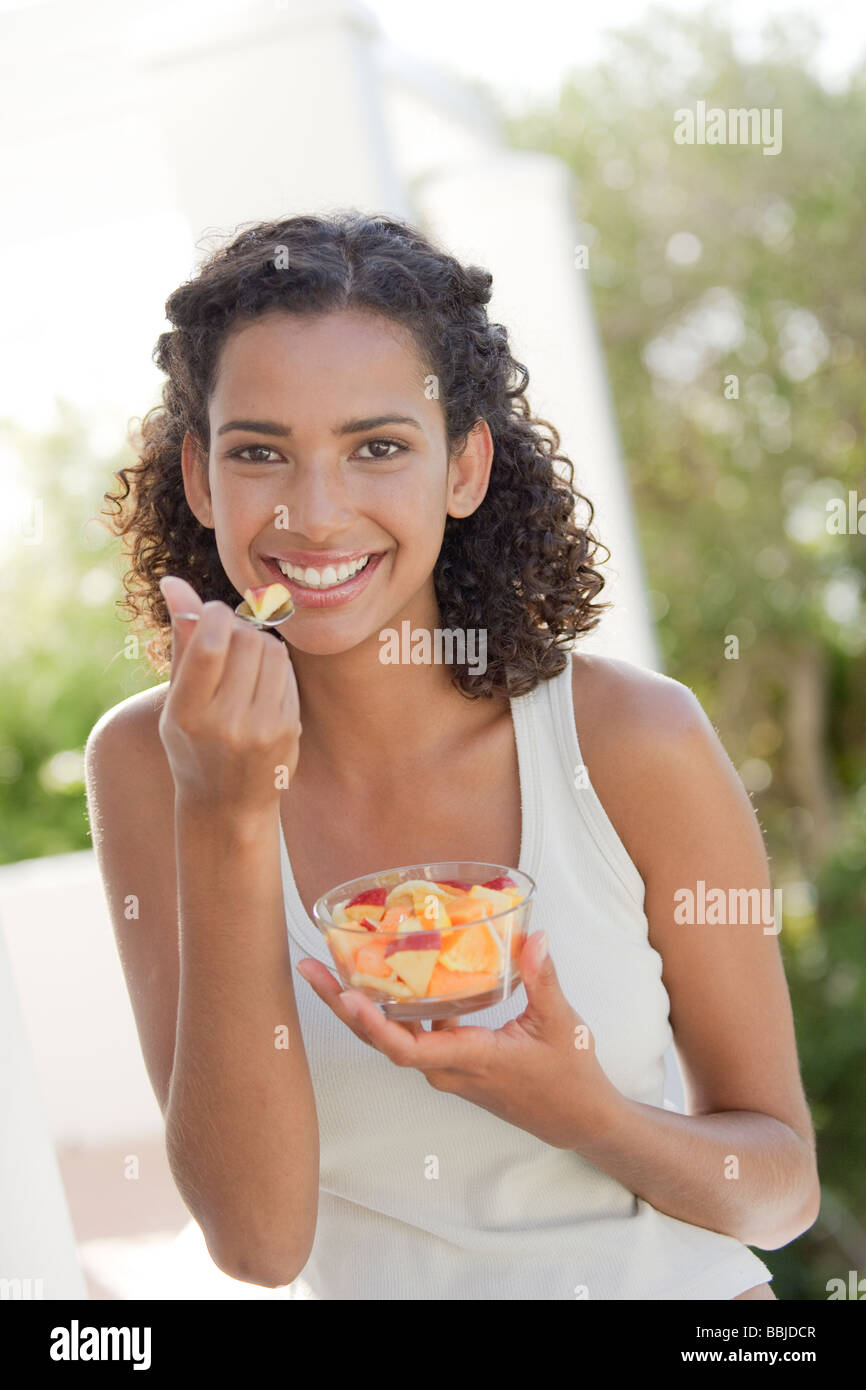 Young smiling woman enjoying fresh fruit salad outdoors on a patio ...