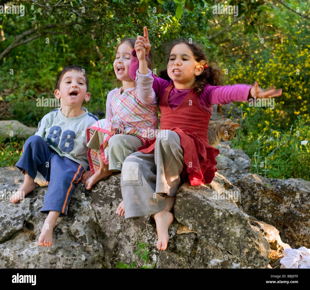 three kids siting on a rock singing outdoors Stock Photo - Alamy