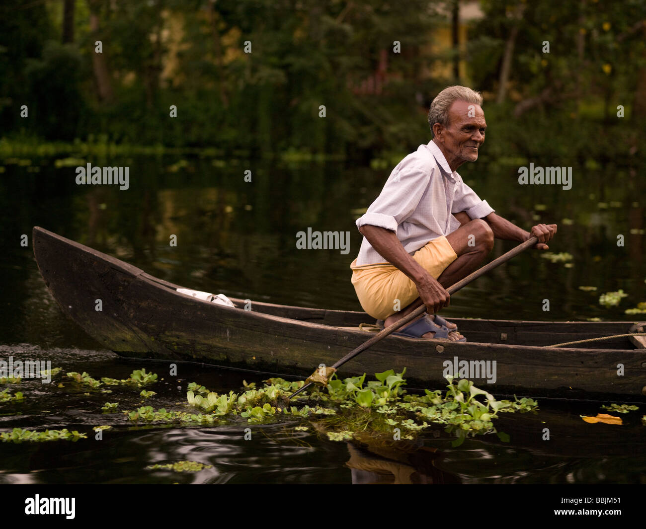 Man crouching in boat holding oar in India Stock Photo - Alamy