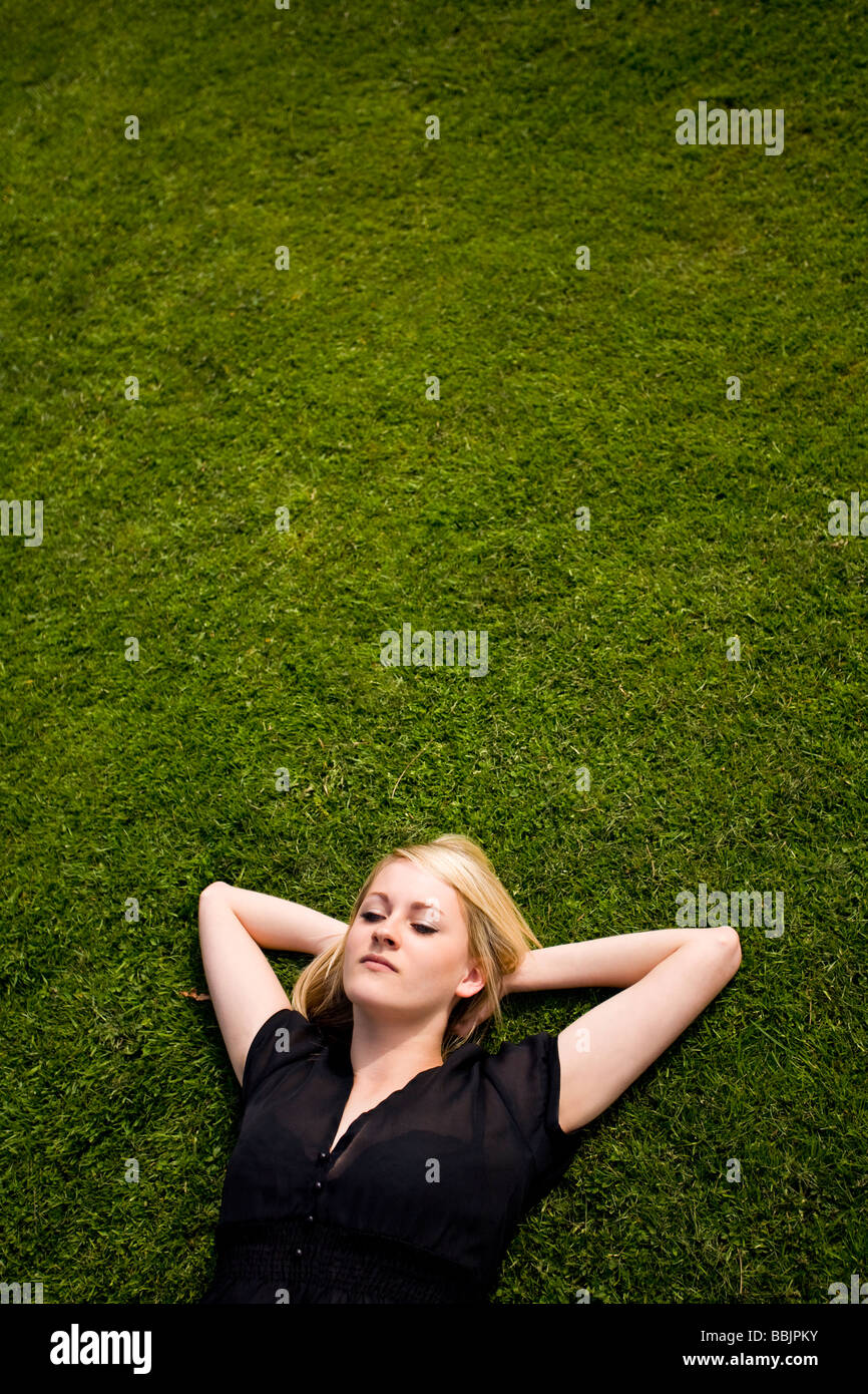 A young woman lies on the grass sunbathing, relaxing, thinking or just ...