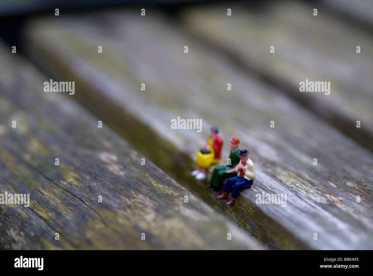 Three Small Figures sat on a bench slat Stock Photo - Alamy