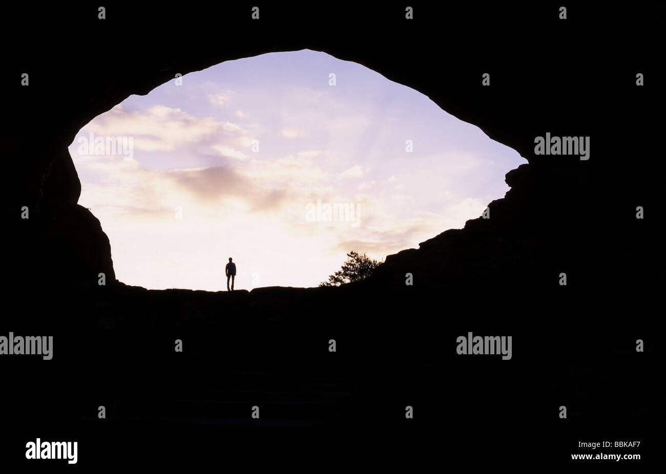 Silhouette of an explorer standing at the entrance to a cave / arch ...
