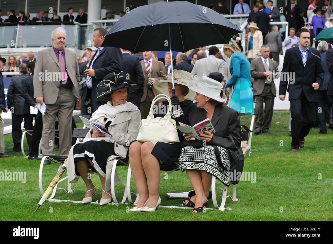 A group of well dressed women sitting on a bench under an umbrella on a ...
