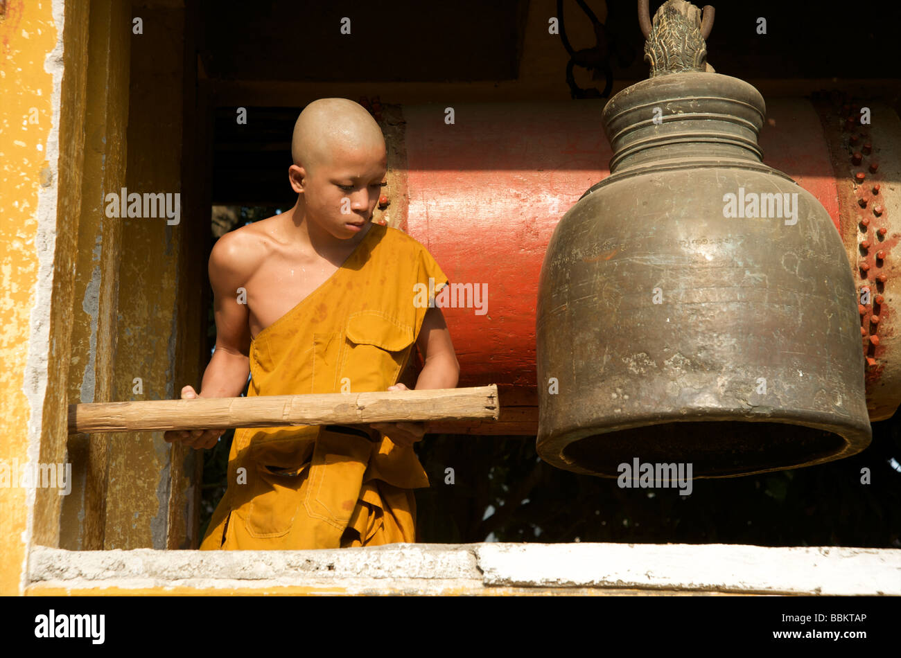 A novice monk calls the monks together by hitting a bell Stock Photo ...