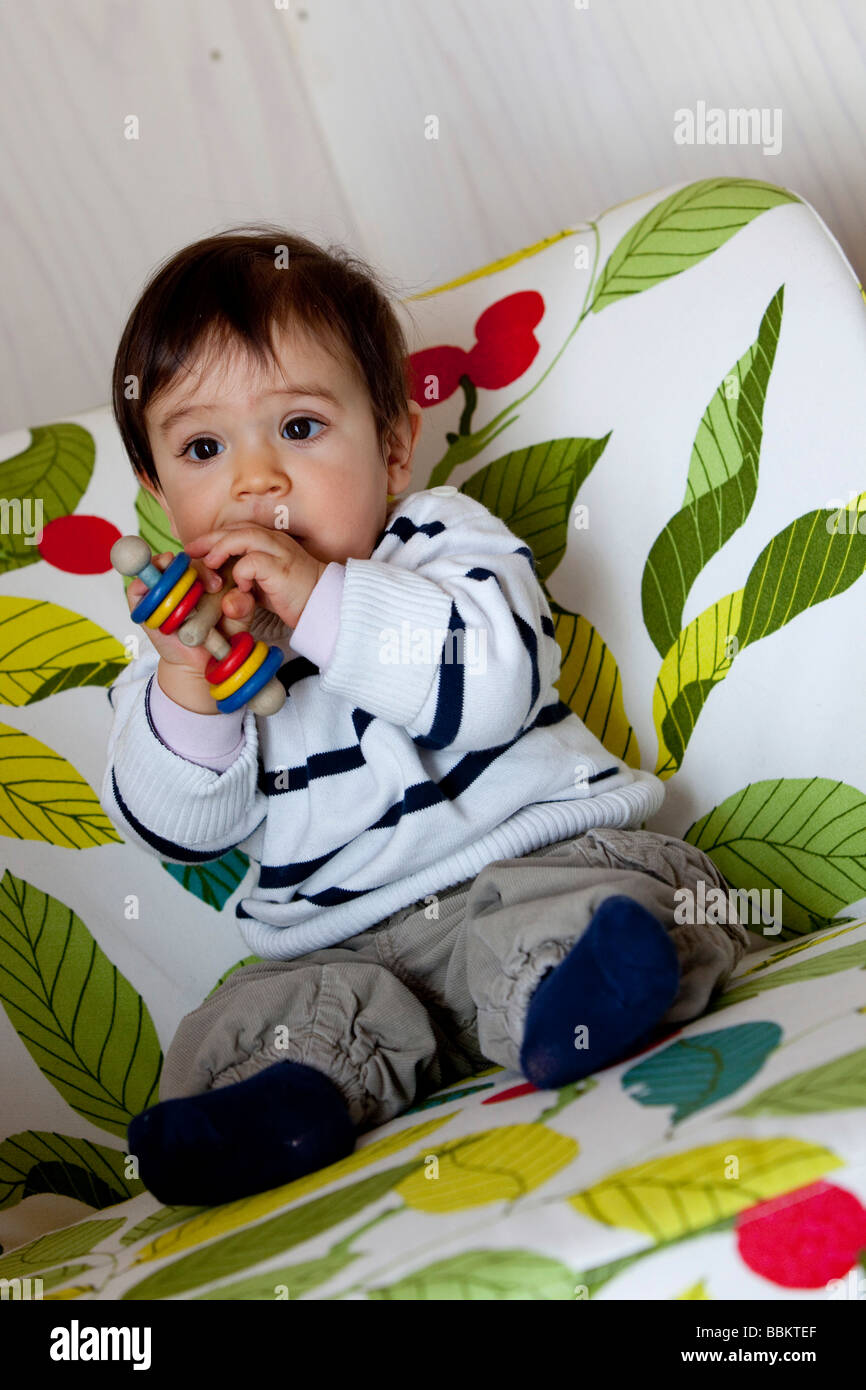 Nine-month-old baby sitting in a chair and biting into a rattle Stock ...