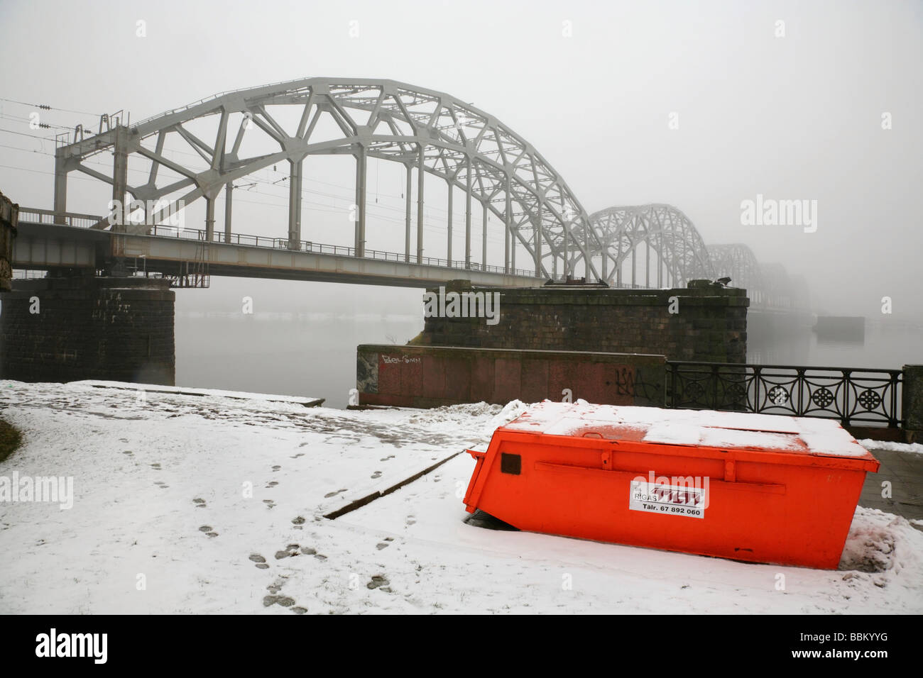 Bright red waste skip near steel arched railway bridge over the River ...