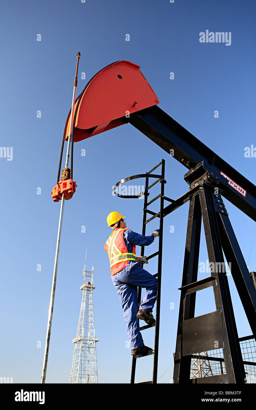 Worker climbing pump jack with oil drilling rig in background at ...