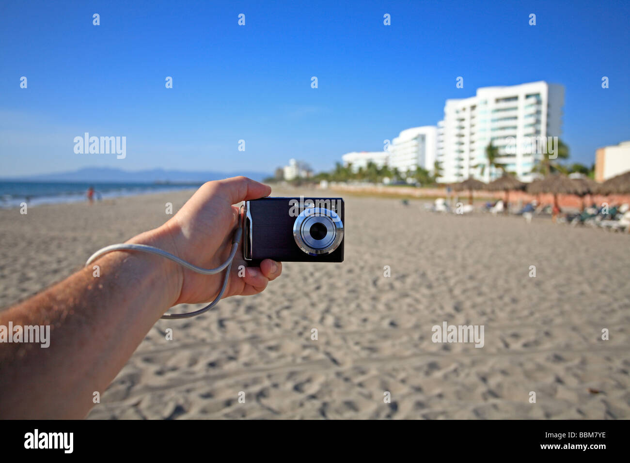 Hand holding compact digital camera taking self portrait at beach at ...