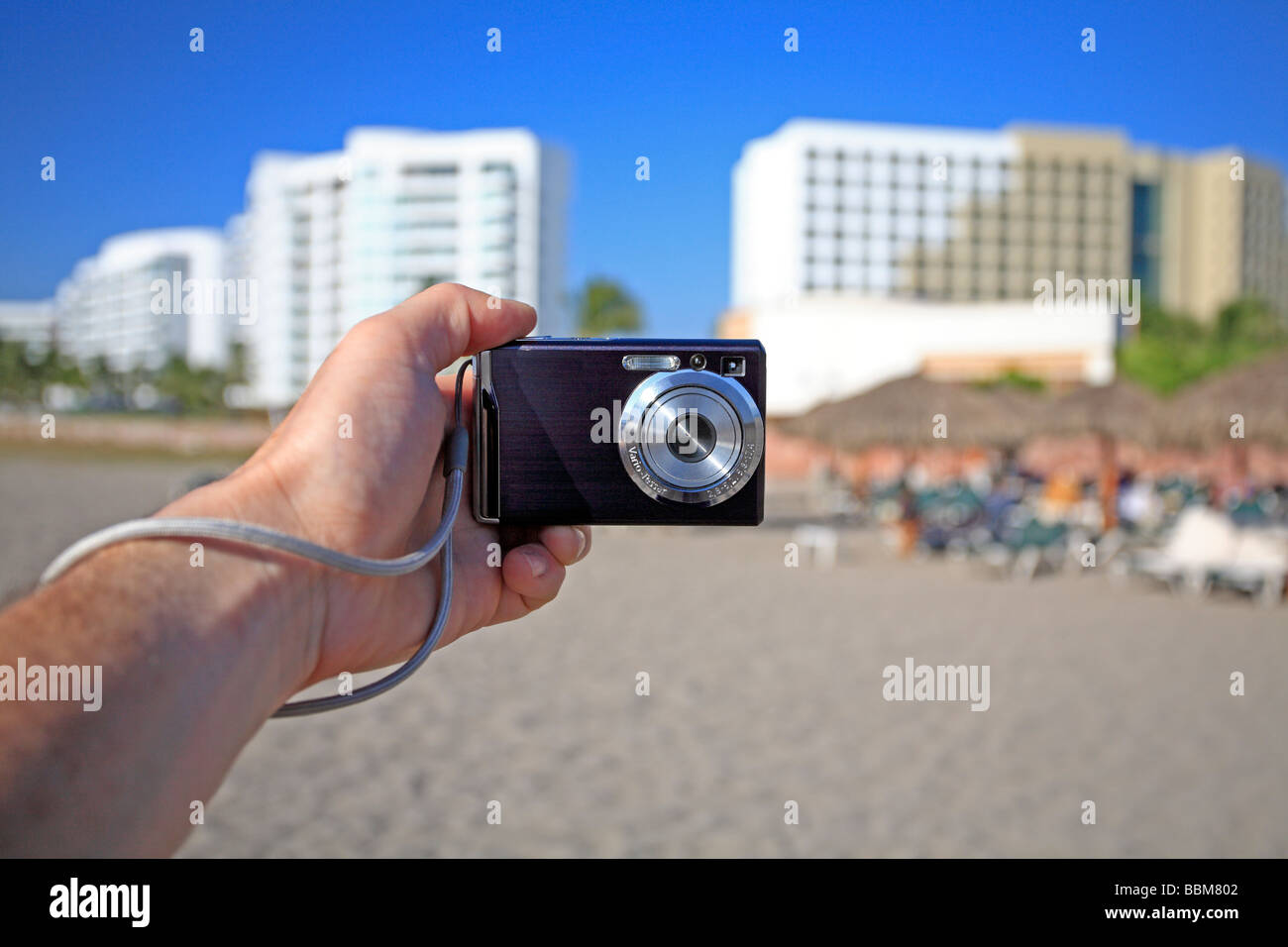 Hand holding compact digital camera taking self portrait at beach at ...