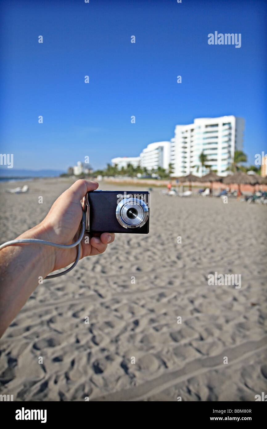 Hand holding compact digital camera taking self portrait at beach at ...