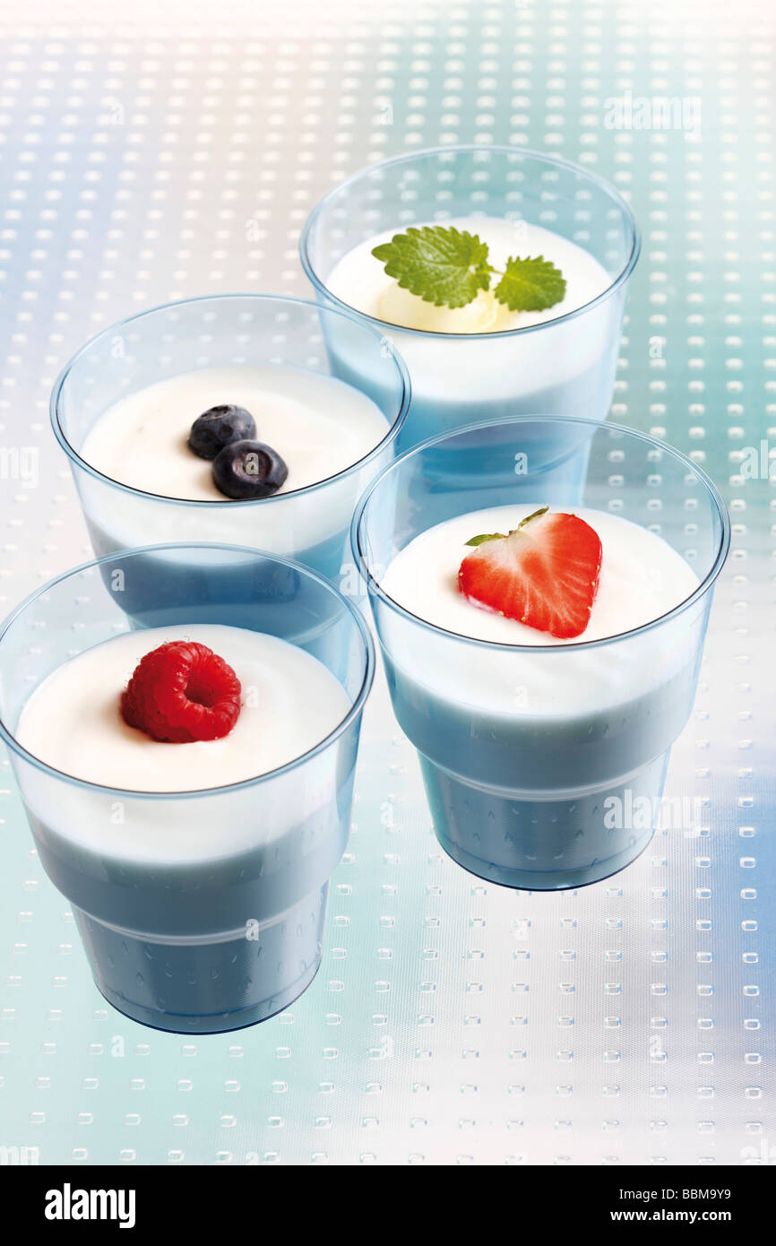 Four blue yoghurt cups with fruit, raspberry, strawberry, blueberries ...