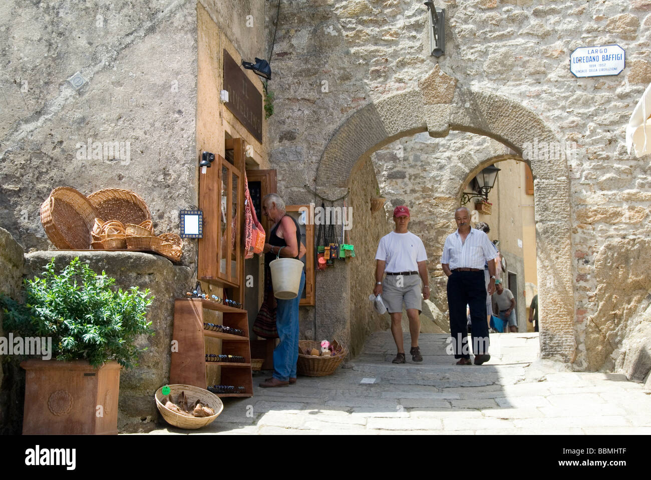 Two men walk through the ancient gate entrance to Giglio Castello Stock ...