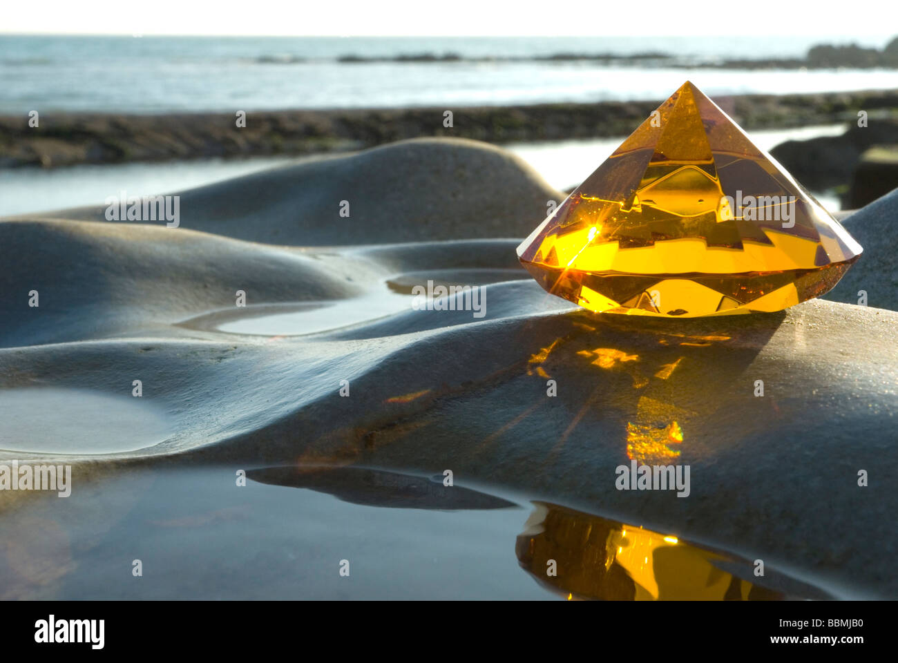 Amber glass pyramid on rock with seawater pool Stock Photo - Alamy