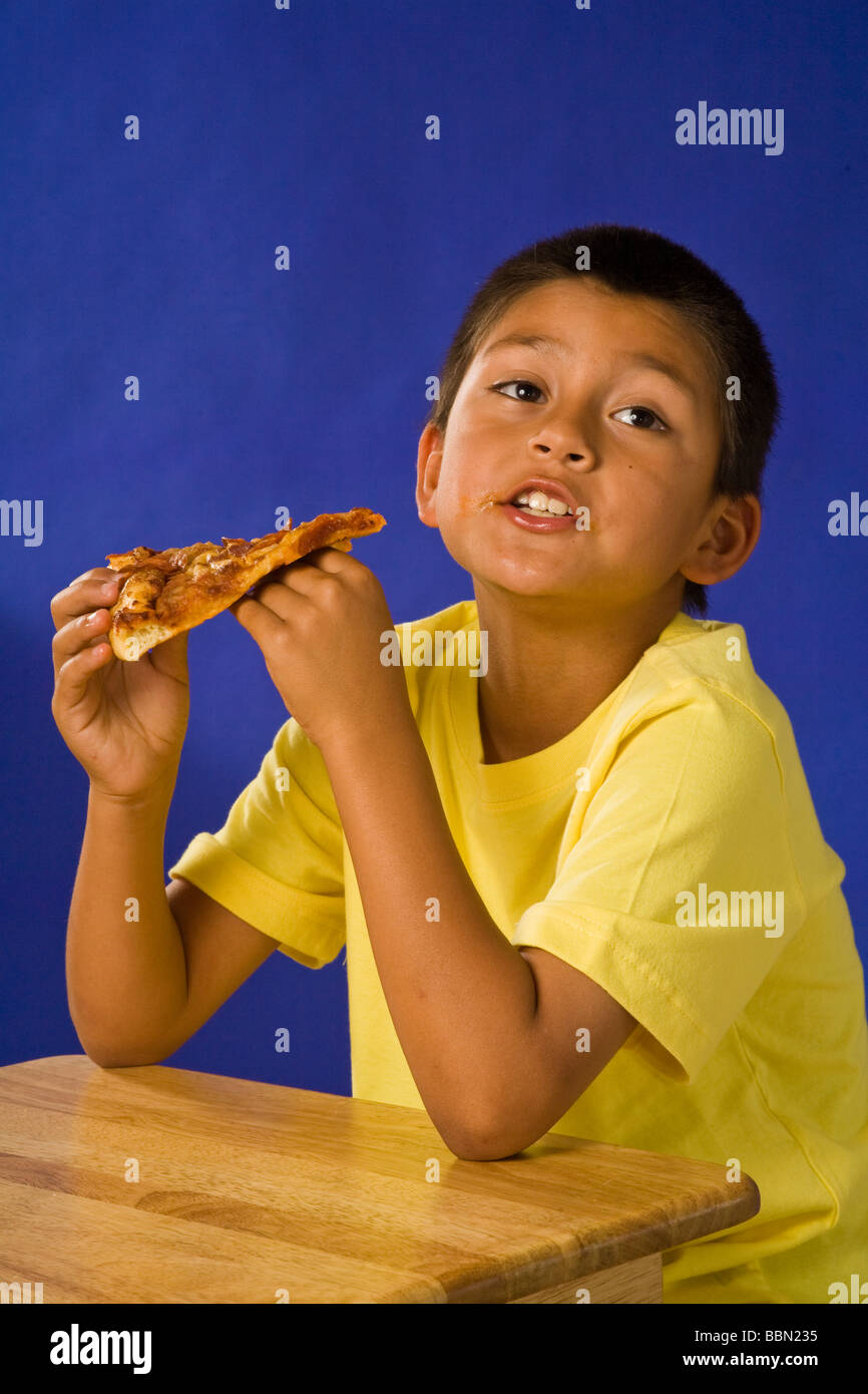 Portrait of young Hispanic boy eating slice of pizza, MR © Myrleen ...