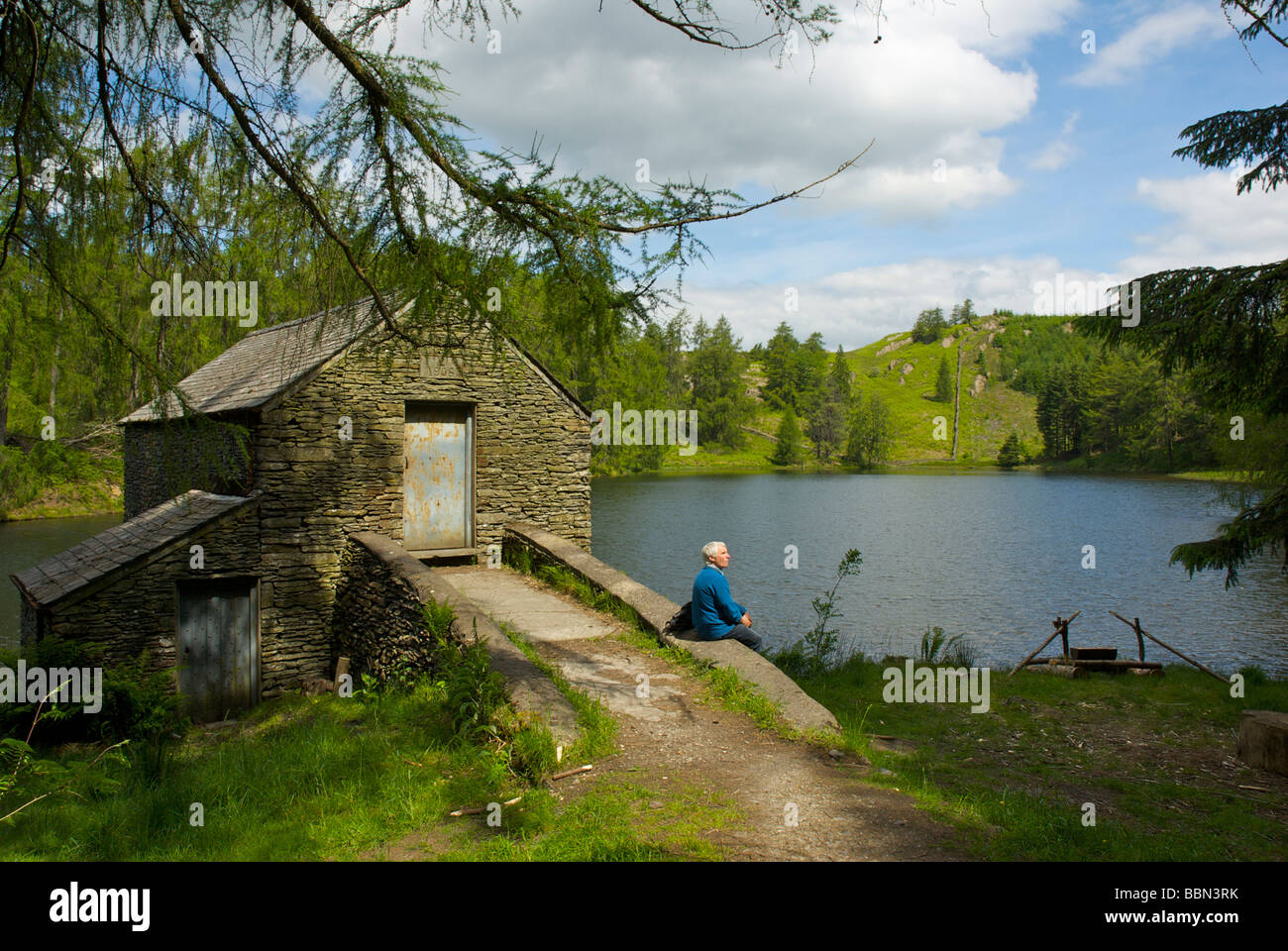 Man sitting by boathouse on Three Dubs Tarn, near Sawrey, Lake District ...