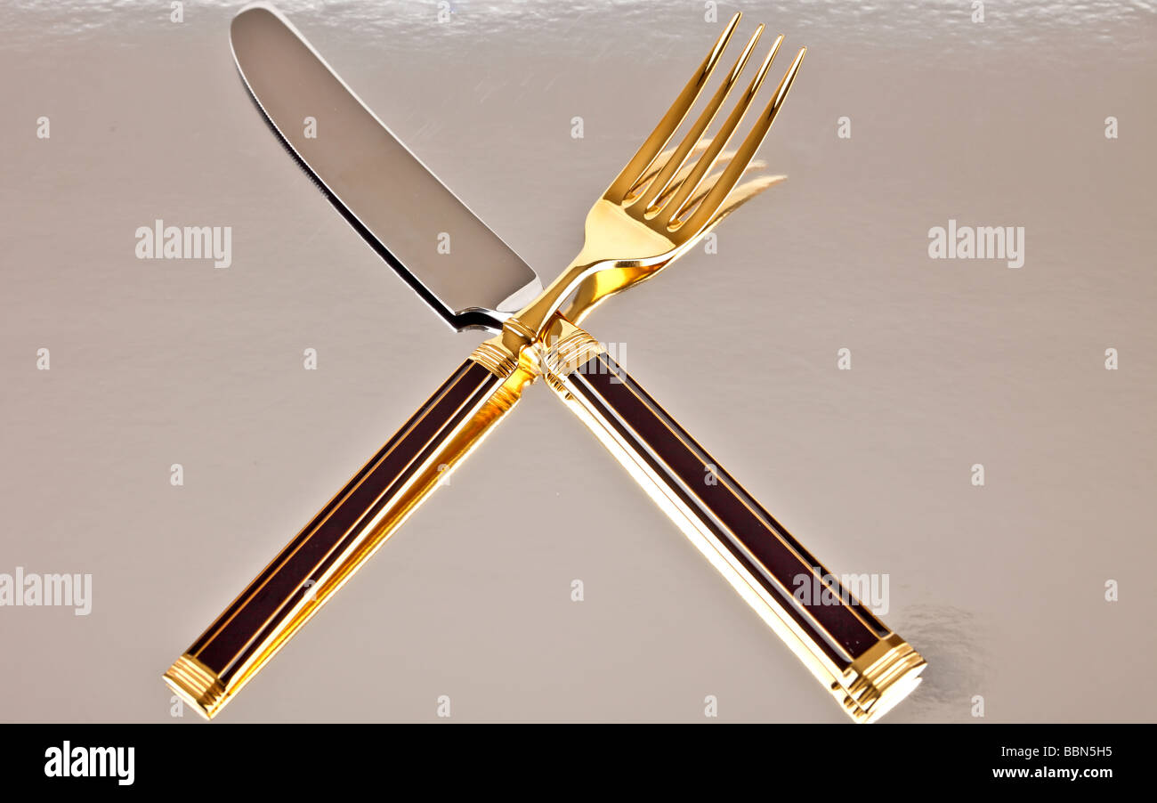 Gold and black knife and fork arranged in a cross on a reflective ...