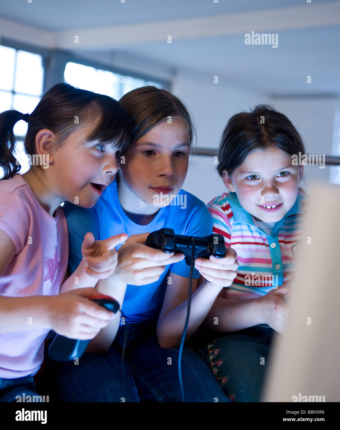 Three little girls intently playing a video game Stock Photo - Alamy