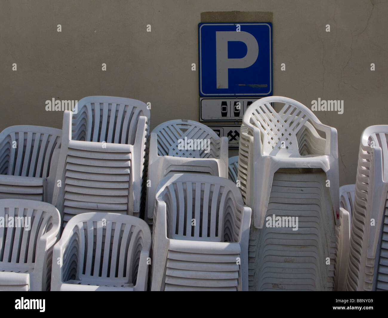Stacked plastic chairs beneath parking sign Stock Photo - Alamy