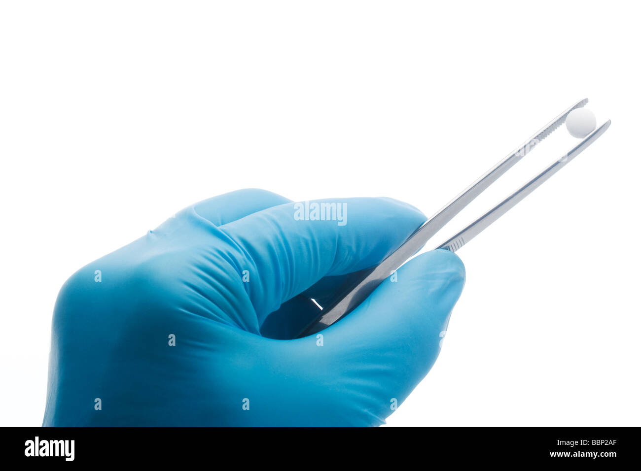 Blue surgical gloved hand holding white pill with tweezer, isolated ...