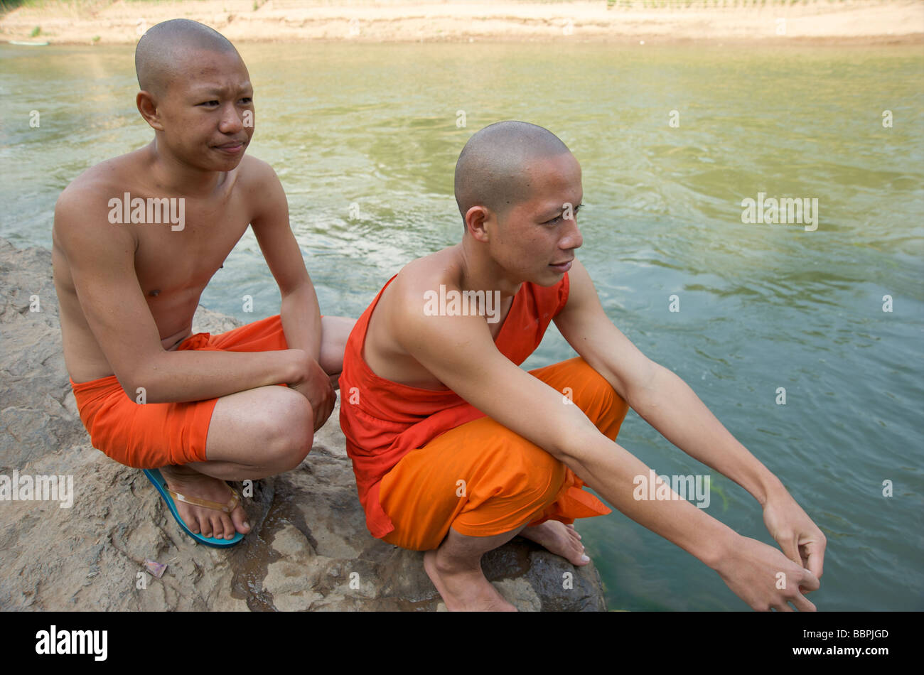 Two Buddhist monks sit on a rock in the Nam Khan river before going for ...
