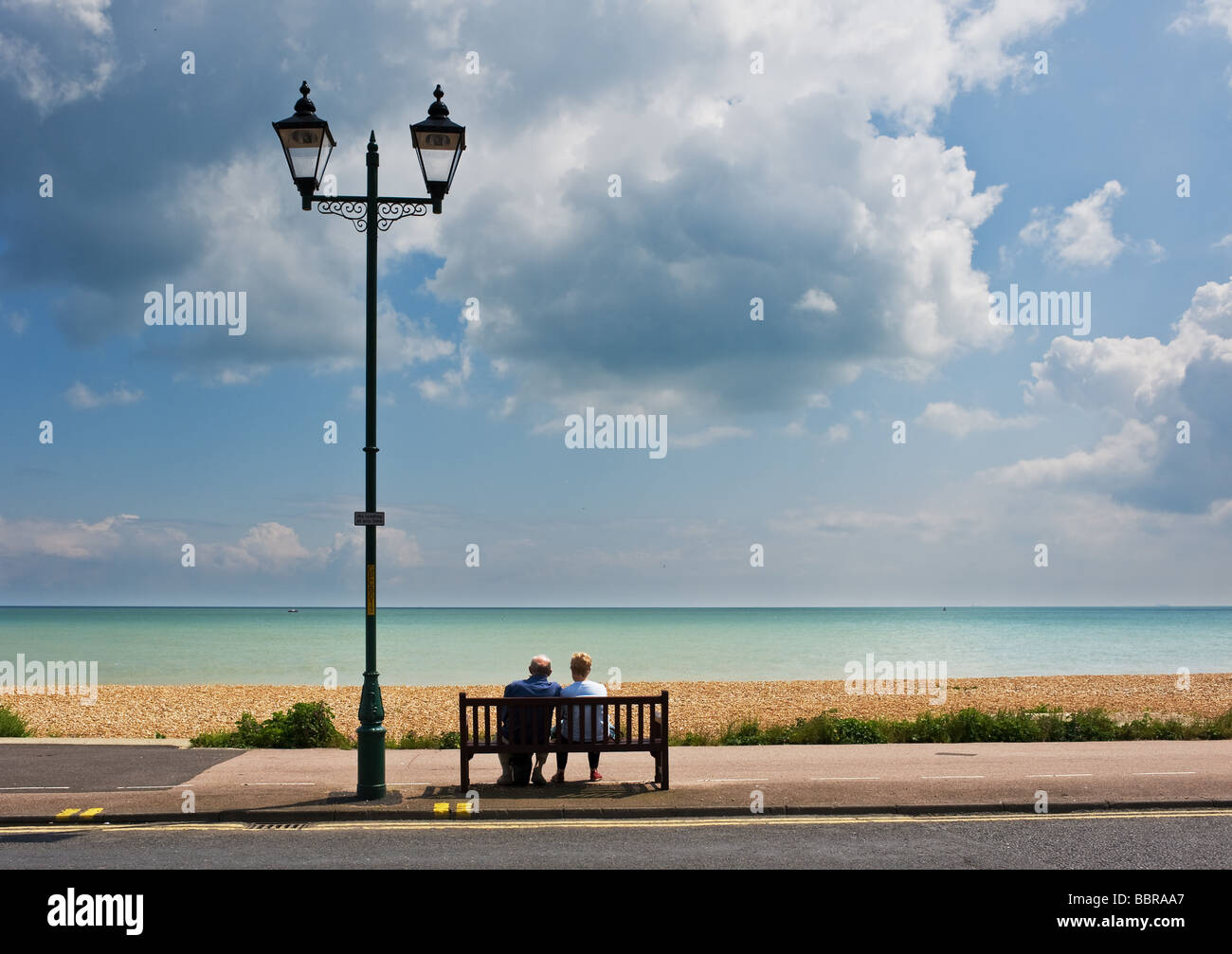 Two elderly people sitting on a bench on the seafront at Deal in Kent ...