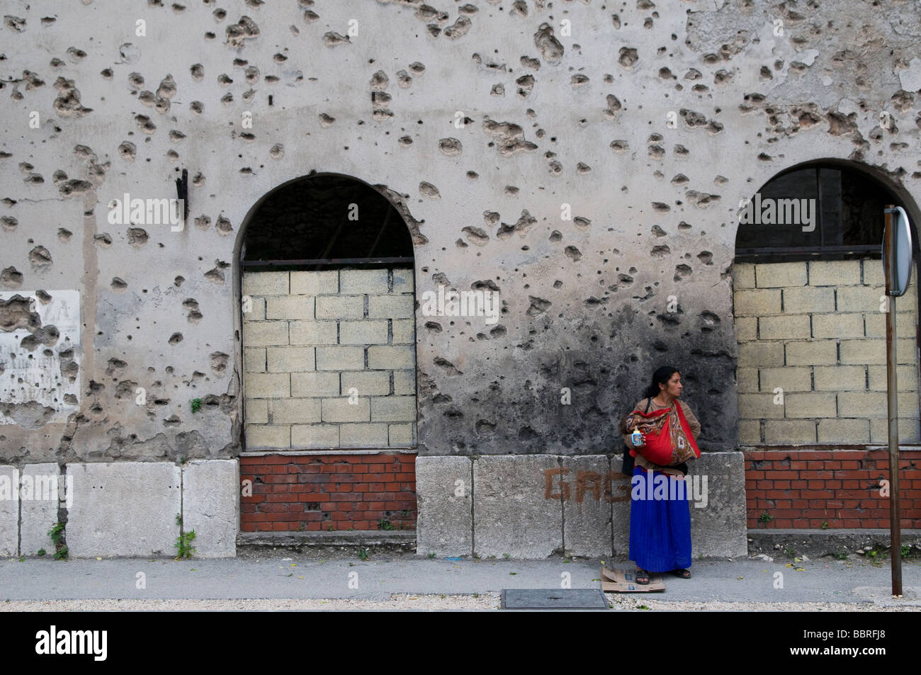 A gypsy woman stands in front of a building riddled with bullet holes ...