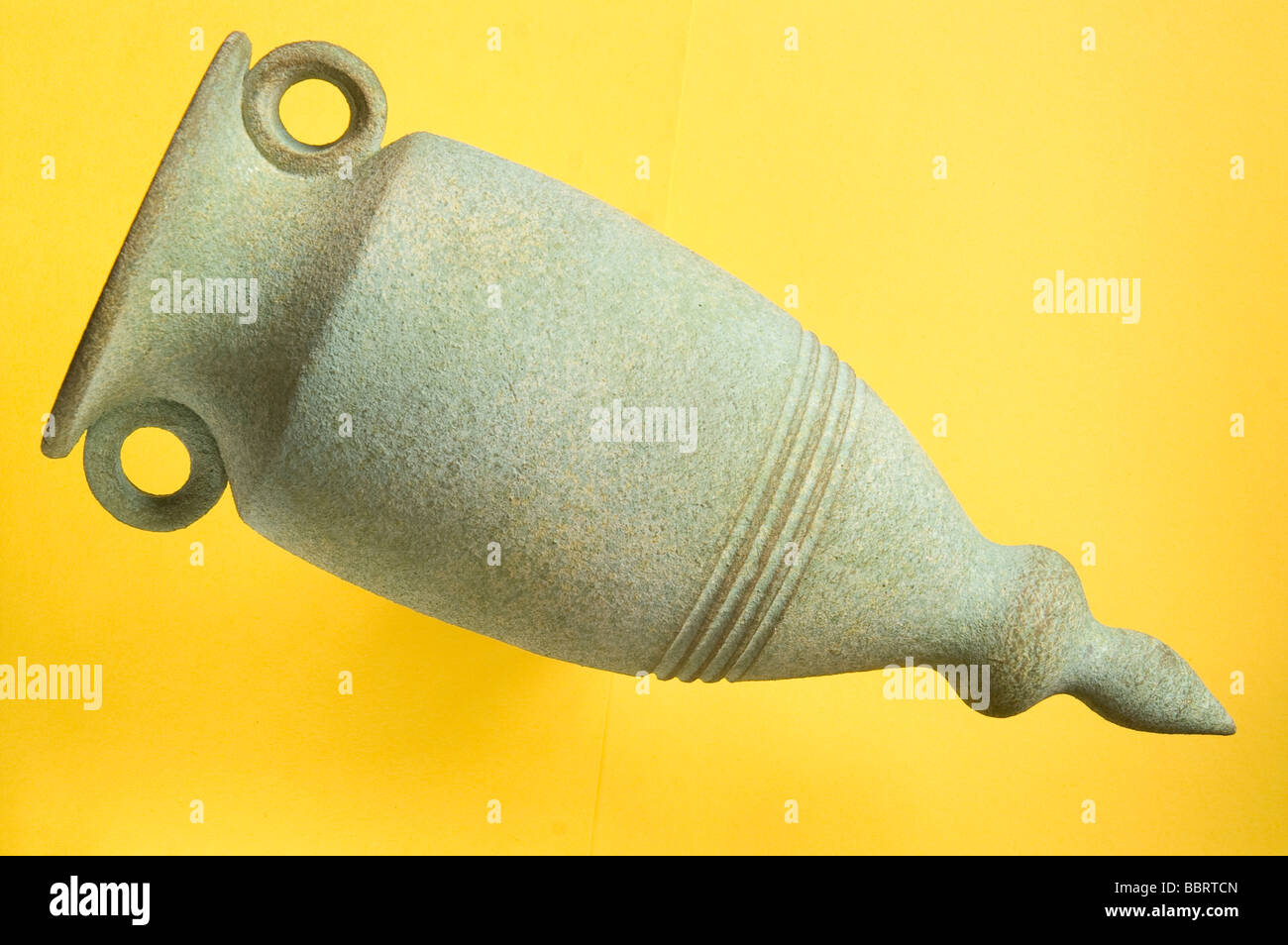 Green clay amphora with side lighting isolated against yellow ...