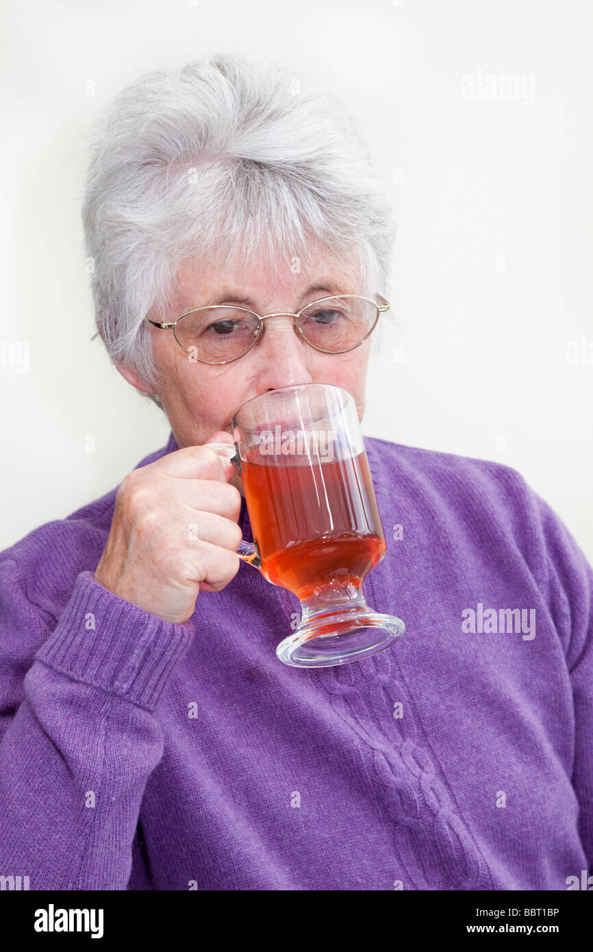 Lonely senior woman looking sad drinking red fruit tea in a glass mug ...