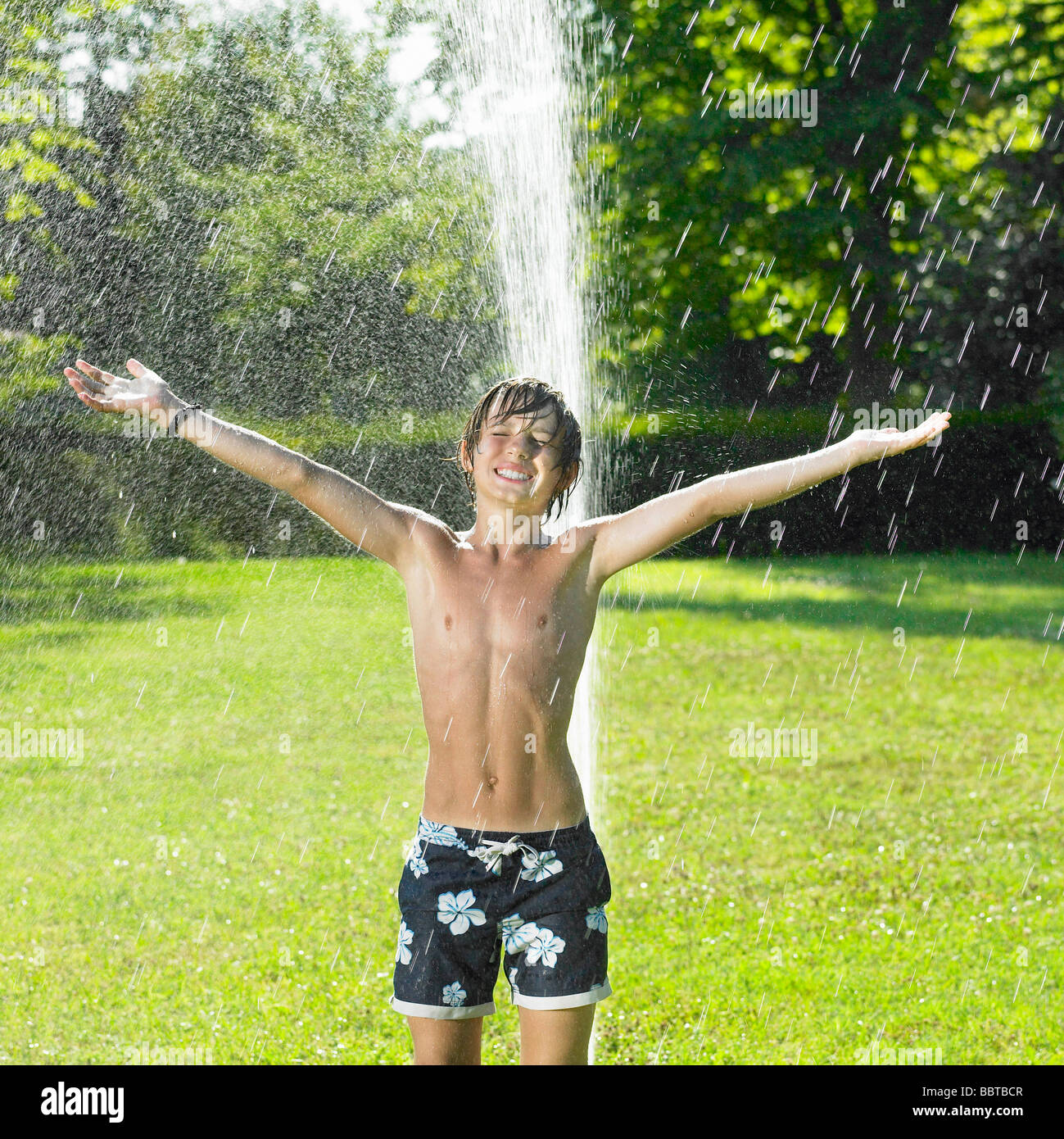 Boy under a water-jet, smiling Stock Photo - Alamy