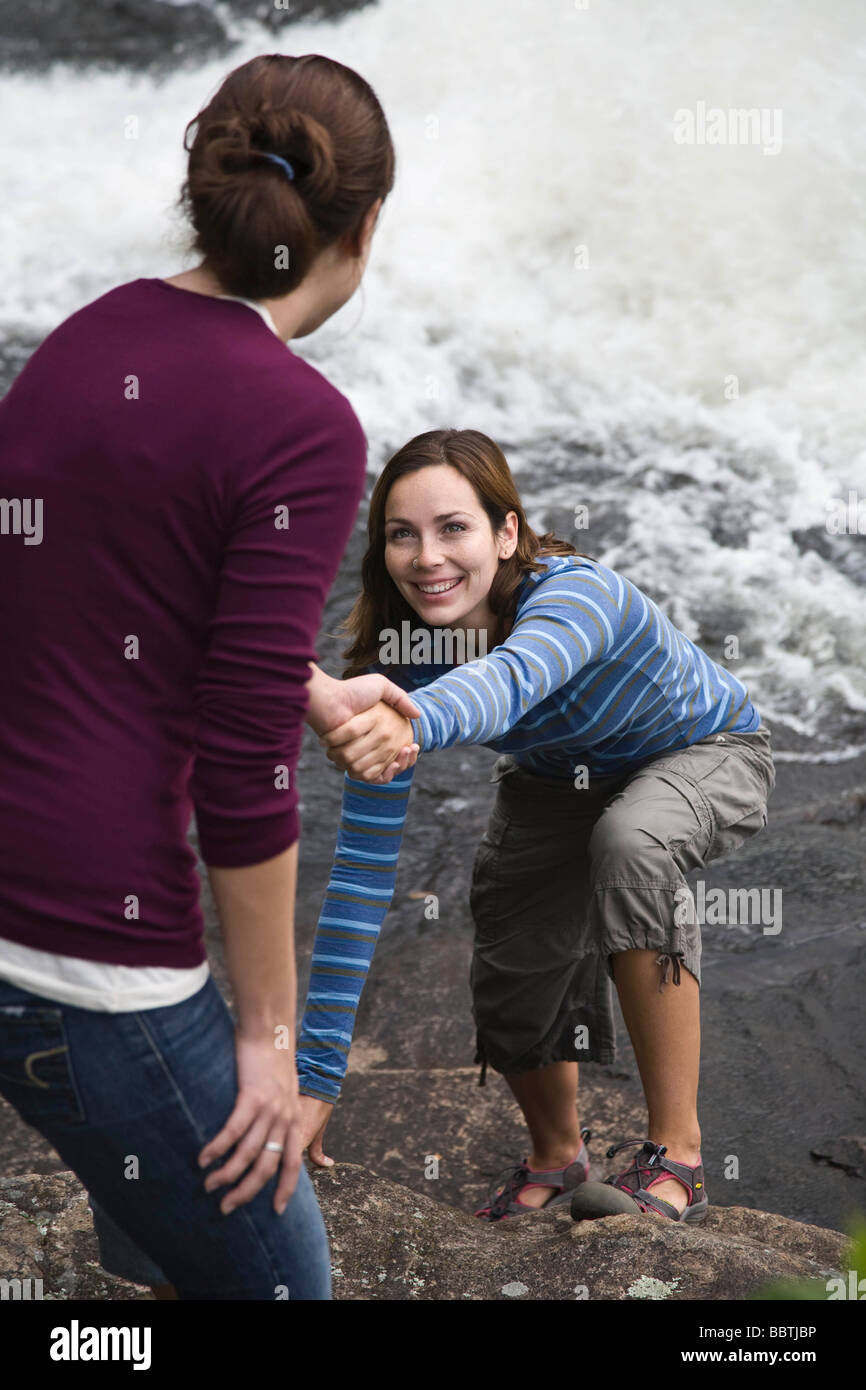 Woman helping friend over rocks Stock Photo - Alamy